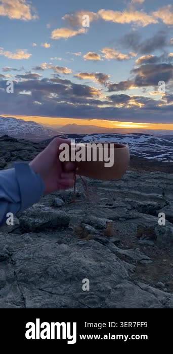 Wooden kuksa cup held above Arctic mountain landscape during sunset in ...