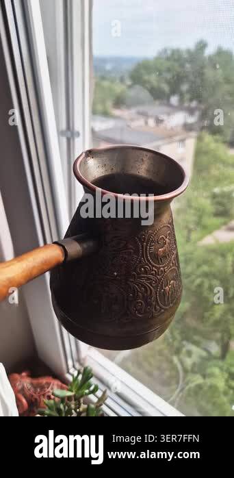 A traditional copper cezve coffee pot filled with dark brew is held ...