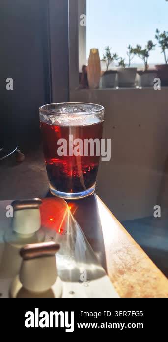 A steaming glass of hot dark loose leaf tea sits by a sunny window ...