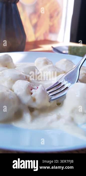 A silver fork lifts a creamy potato gnocchi from a white plate in a ...