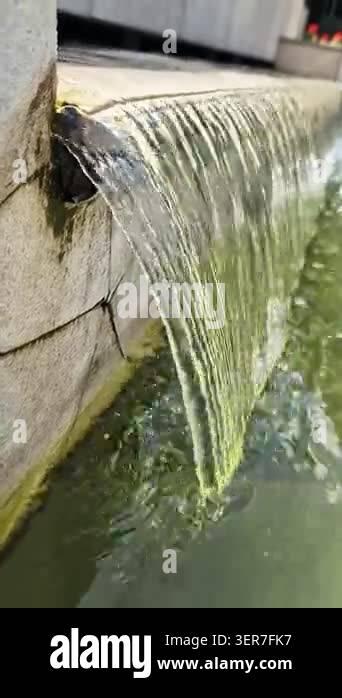 Clear water flows continuously over a textured stone fountain ledge ...
