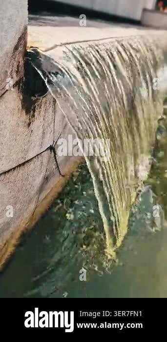 Clear water cascades smoothly over a textured stone ledge into a ...