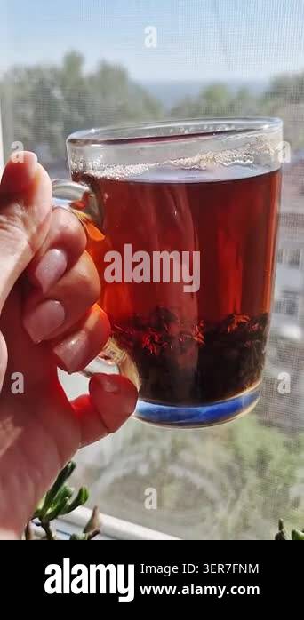 A close-up view of a hand with manicured nails holding a clear glass ...