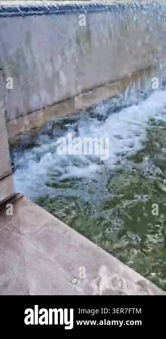 Clear water flows smoothly over a textured concrete ledge, splashing ...