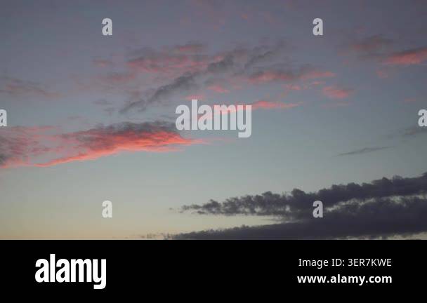 A panning evening shot tracks gorgeous pink clouds scattered across a ...