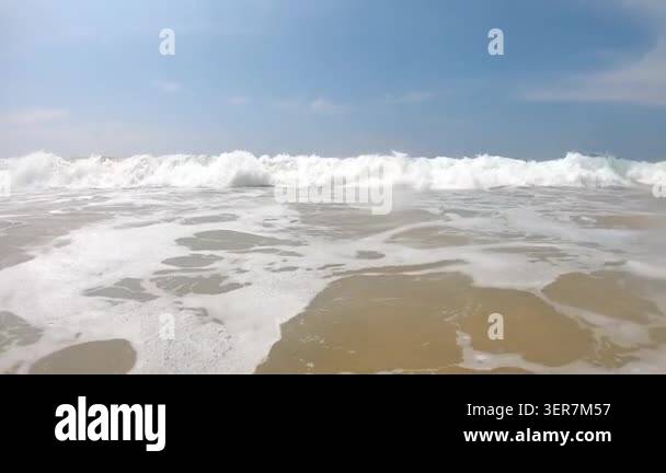 Ocean waves crash onto the sandy shore, with a hand reaching into the ...