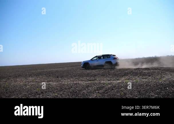 Vehicle maneuvers through an expansive field, creating a cloud of dust ...