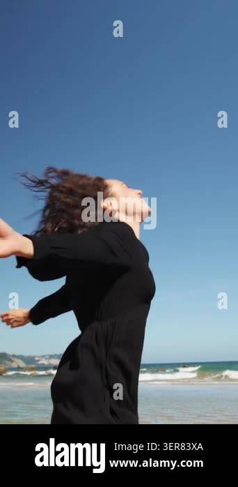 Carefree woman in a black dress laughing and spinning with joy on a ...