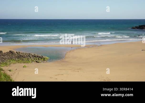 A solitary woman in a long black dress stands on a vast sandy beach ...