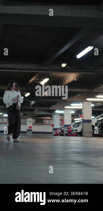 A young woman walks quickly through an underground parking garage ...