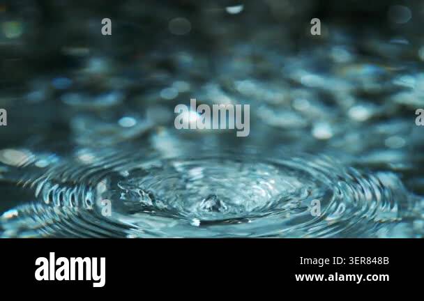 Macro close-up of a falling water drop creating a splash and ripples on ...