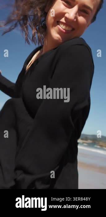 A happy woman in a black dress runs and dances on a sandy beach on a ...