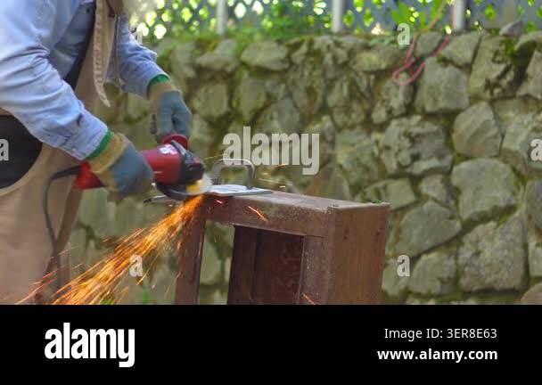 An older man with a long white beard using a red angle grinder to cut ...