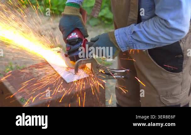 A worker wearing safety gloves uses an angle grinder to cut a metal ...