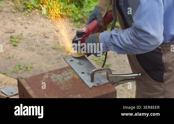 Worker using an angle grinder to smooth and cut a metal plate securely ...