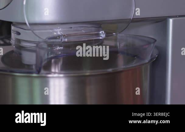 Close-up shot of flour being poured into a spinning stand mixer bowl ...