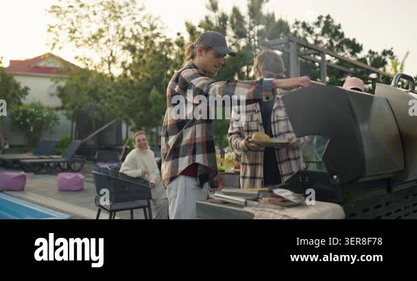 A young man stands by a large outdoor grill preparing food for a ...