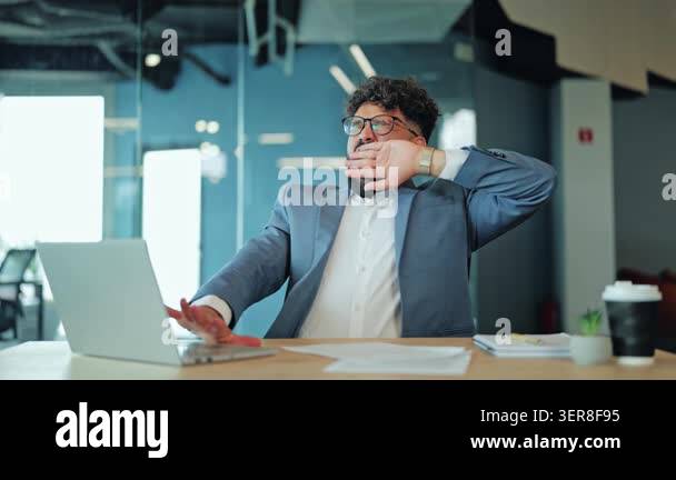Overworked Middle Eastern executive sits at office desk, yawning from ...