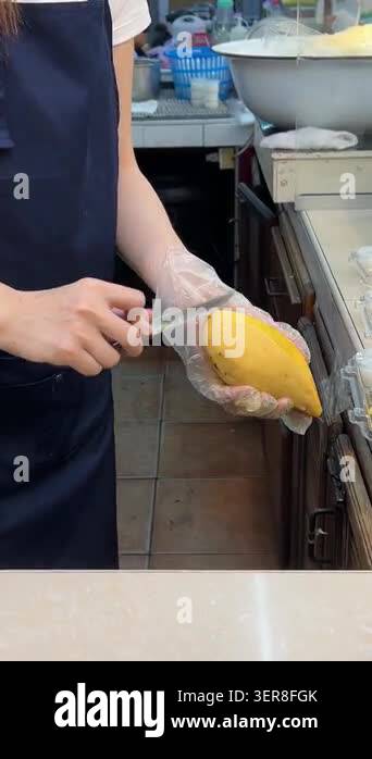 Close up of street vendor hands peeling a fresh ripe yellow mango for ...