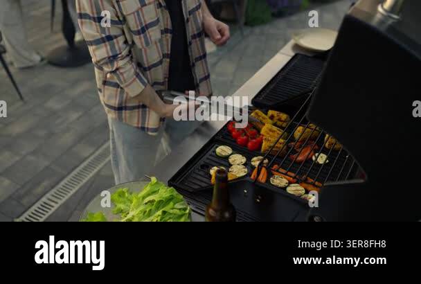 Adult man prepares a colorful mix of vegetables on a barbecue grill ...