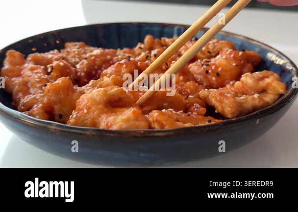 A person uses chopsticks to pick up and enjoy a chicken wing coated in ...