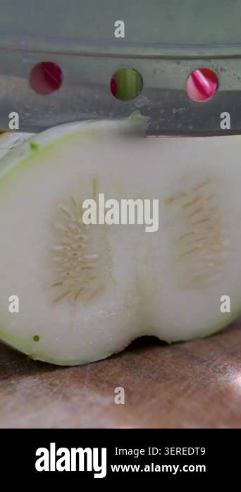 Fresh pattypan squash is being sliced on a wooden cutting board ...