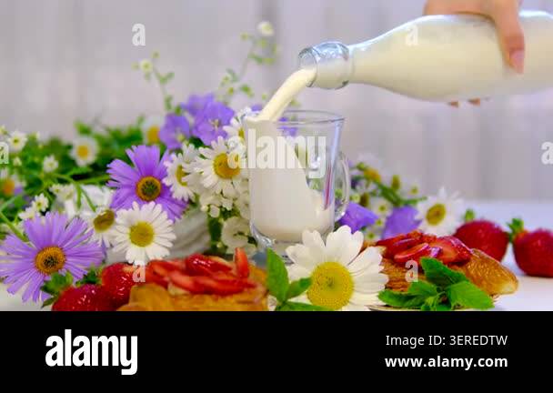 Fresh milk is poured into a clear glass next to strawberry puff pastry ...