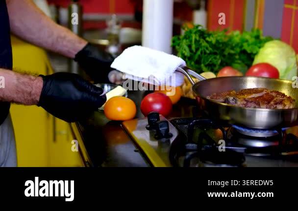 Chef in black gloves seasons, sears and bastes a ribeye steak with ...