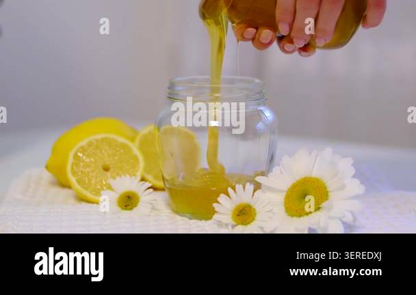 Golden flower honey flows into a glass jar beside fresh chamomile ...
