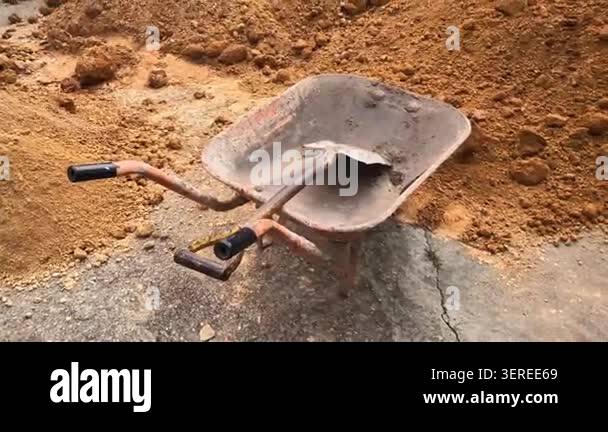 Wheelbarrow placed beside piles of soil at a construction site. Manual ...