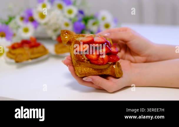 Female hands hold a flaky puff pastry filled with fresh strawberries ...