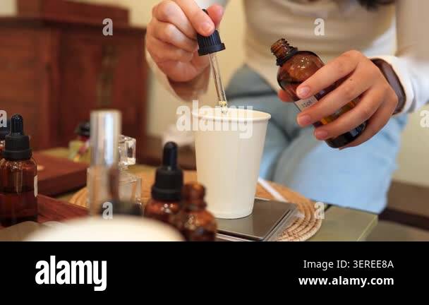 Close-up of a dropper dispensing essential oil into a mixing container ...