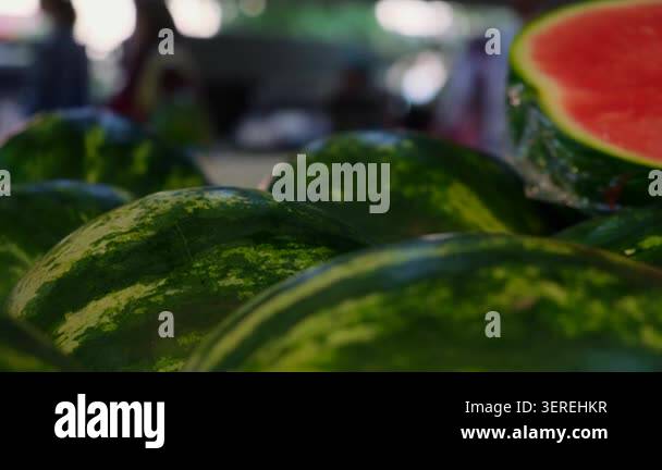 Closeup watermelons on market table, glossy green rinds and halfcut red ...