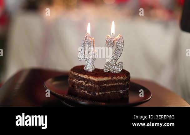 A slice of heart-shaped cake on a plate with lit candles in the shape ...