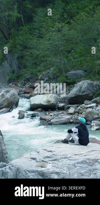 A solitary traveler pauses by a gushing river amidst a rocky landscape ...