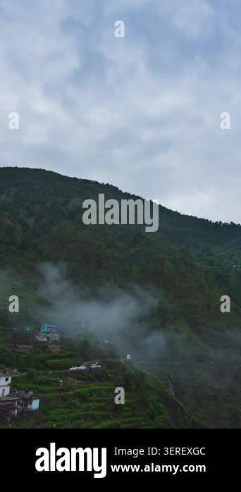 A serene village nestled on a lush green mountain slope shrouded in ...