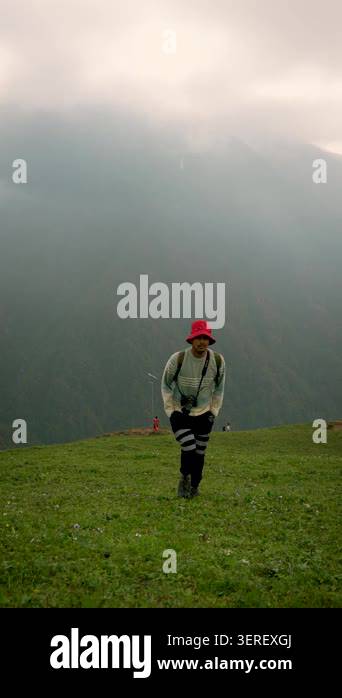 A lone traveler in a red hat walks on a verdant hillside, exploring the ...