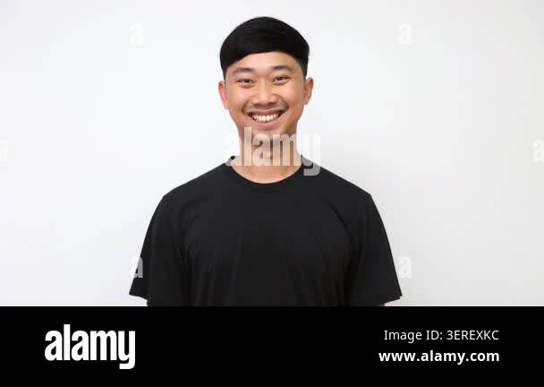 young Asian man in a plain black t-shirt smiles widely and happily ...