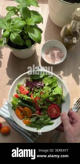 Person's hand placing a bowl of fresh salad with tomatoes on a wooden ...