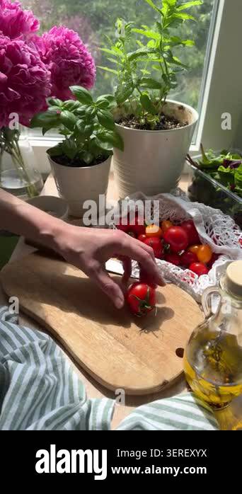 Woman's hands taking fresh cherry tomatoes from a mesh bag to prepare a ...
