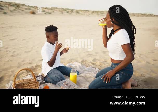 African American mother and son enjoying a seaside picnic on sandy ...