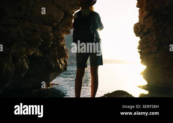 Young woman with backpack enjoying quiet moment inside sea cave ...