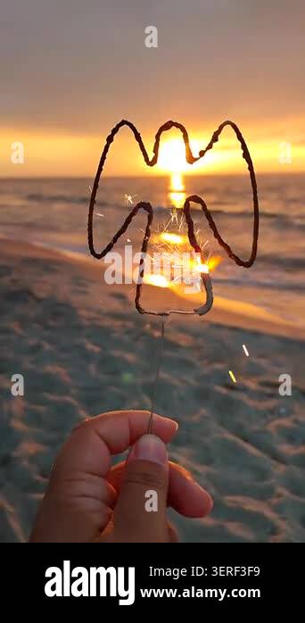 Burning sparkler in shape of angel against backdrop of sea at sunrise ...