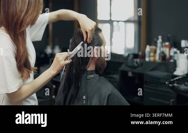 Female barber cutting long wet hair of male client with scissors and ...