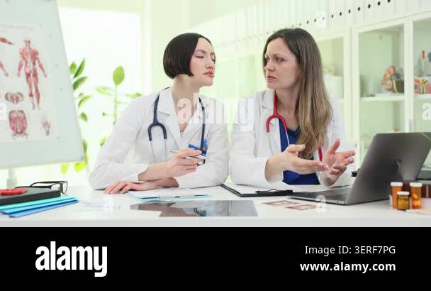 Pair of women doctors discusses patient records at clinic desk ...