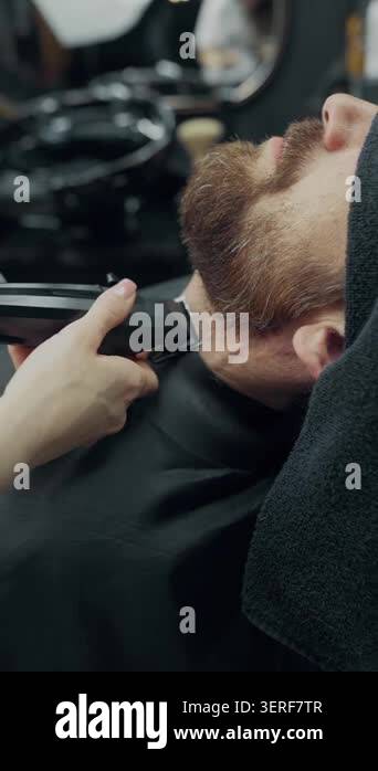 Professional female barber trimming beard of male client with electric ...