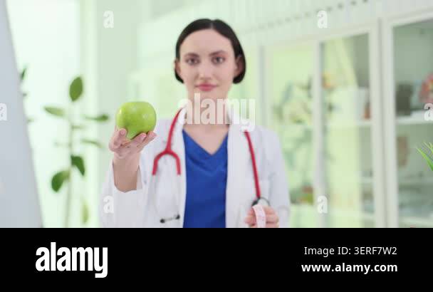 Happy woman doctor holds apple and tape measure over desk in hospital ...