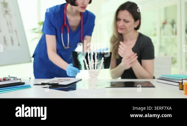 Human wrist and hand bones model and doctor shows x-ray image to lady ...