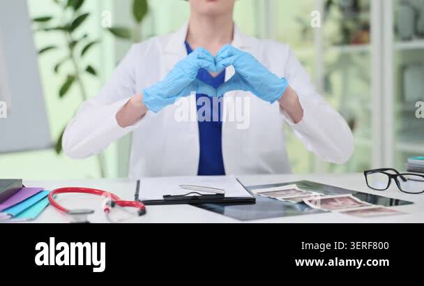 Woman cardiologist shows heart with hands sitting in workplace. Female ...