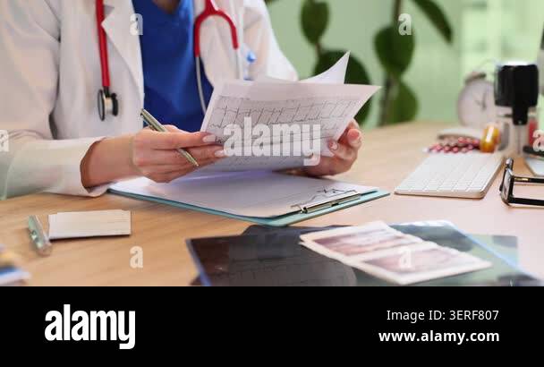 Woman doctor reads patient cardiogram as sits at workplace. Female ...